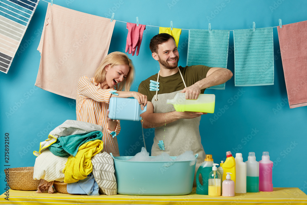 young hardworking couple enjoying washing clothes, expressing positive ...