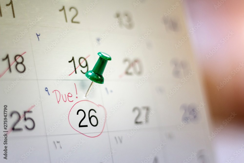 Due date of payment written on a calendar with a green push pin to ...