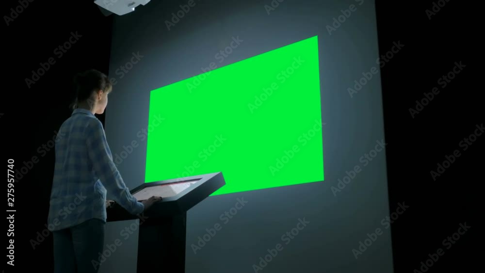 Woman looking at blank large interactive wall green display in dark ...