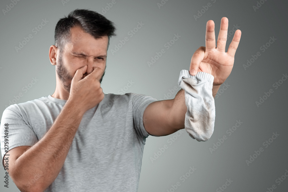 A Young Man Holds His Smelly Socks And Covers His Nose With His Hand