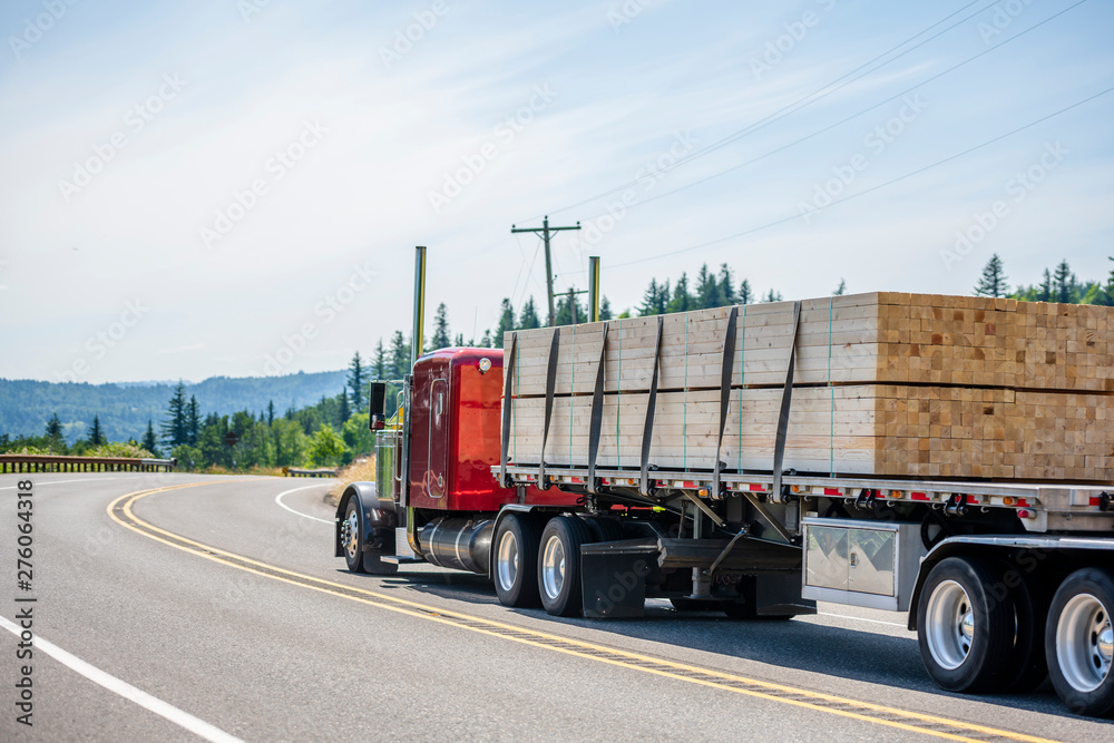 Red big rig semi truck transporting wood lumber on the flat bed semi ...