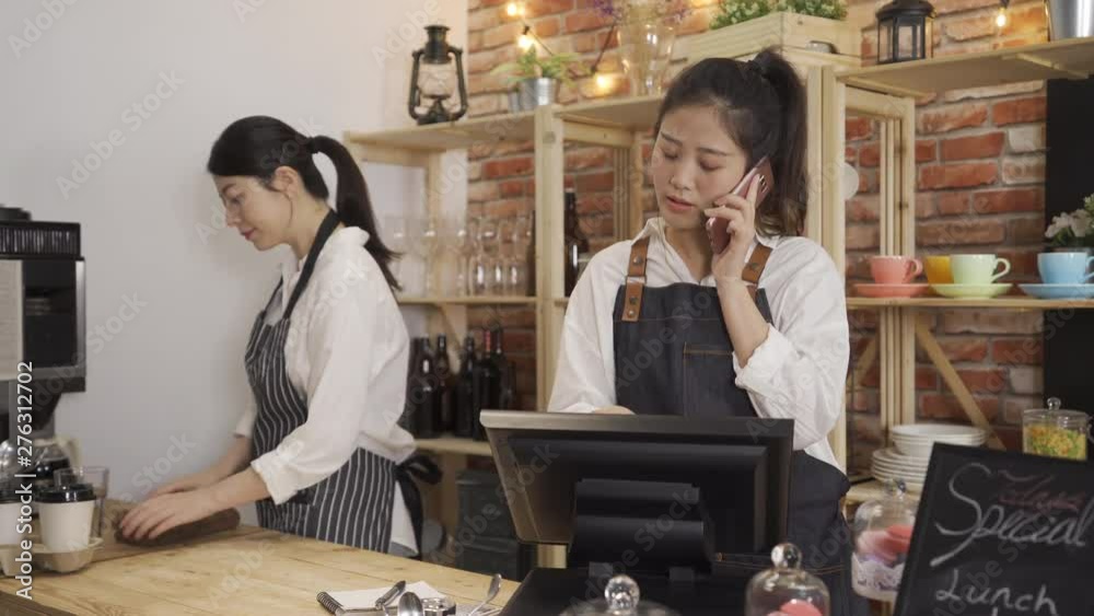 Two asian women baristas working in cafe bar together standing in counter. waitress preparing ...