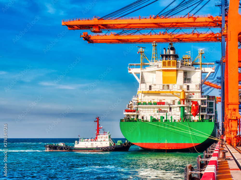 A tugboat pushing a container vessel during berthing at an industrial ...
