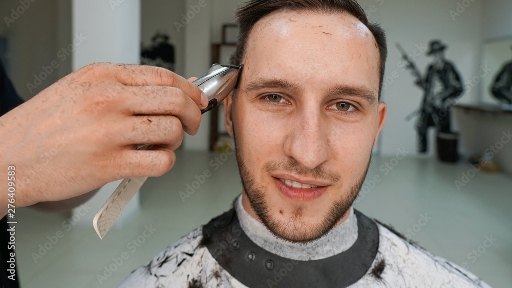 portrait of happy young man being trimmed with professional electric ...