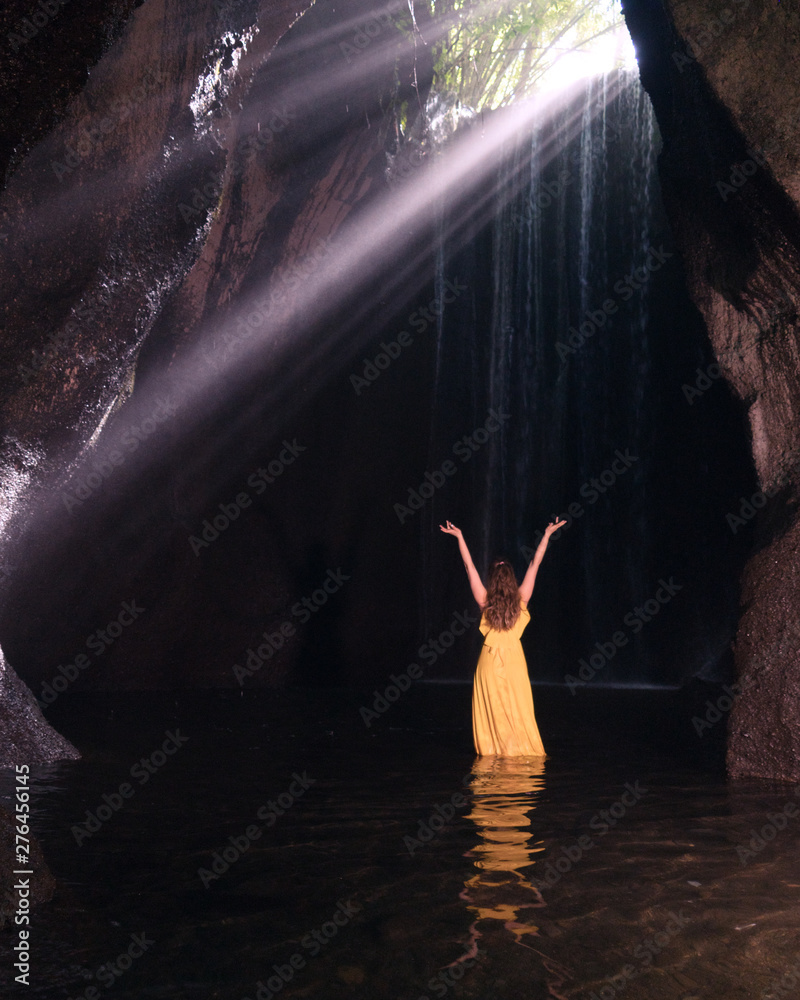 Famous Bali waterfall in the cave Tukad Cepung. Young girl in yellow ...