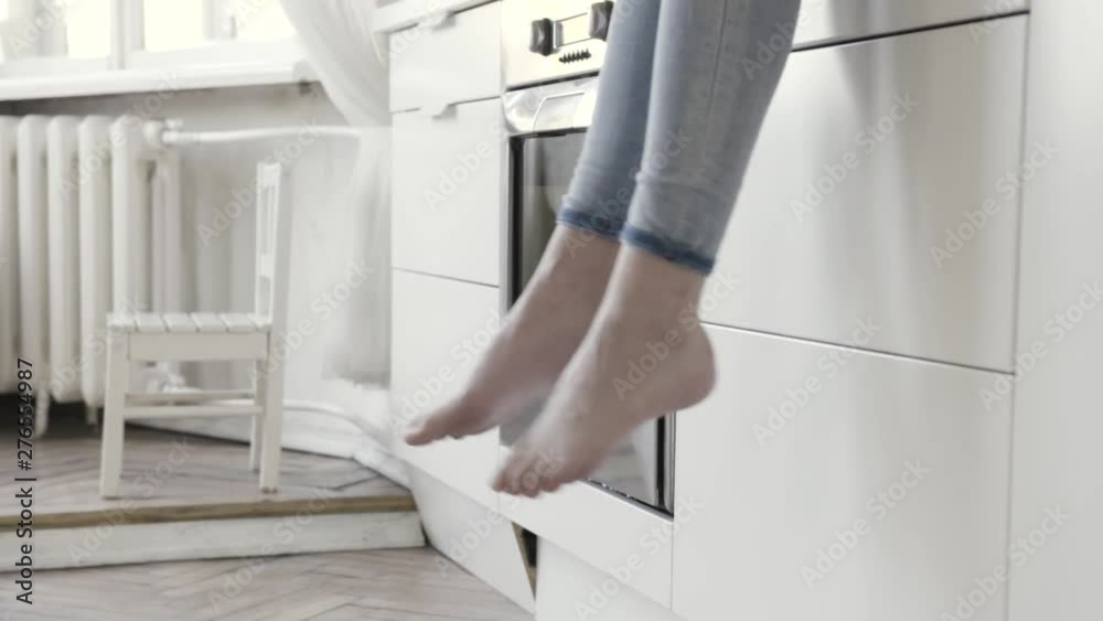 Close up for woman legs dangling with white kitchen drawers and oven on ...