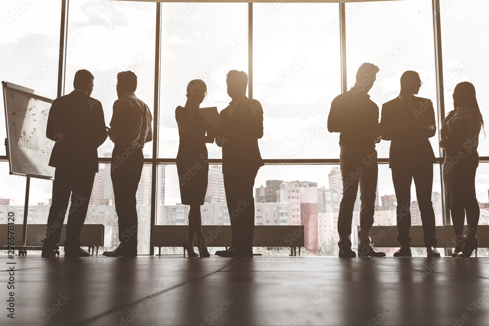 Silhouettes of people against the window. A team of young businessmen ...