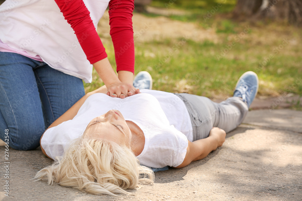 Female passer-by doing CPR on unconscious mature woman outdoors Stock ...