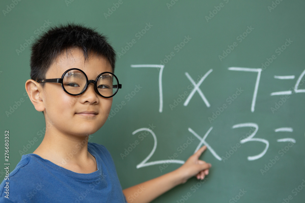 Schoolboy doing math on greenboard in a classroom Stock Photo | Adobe Stock