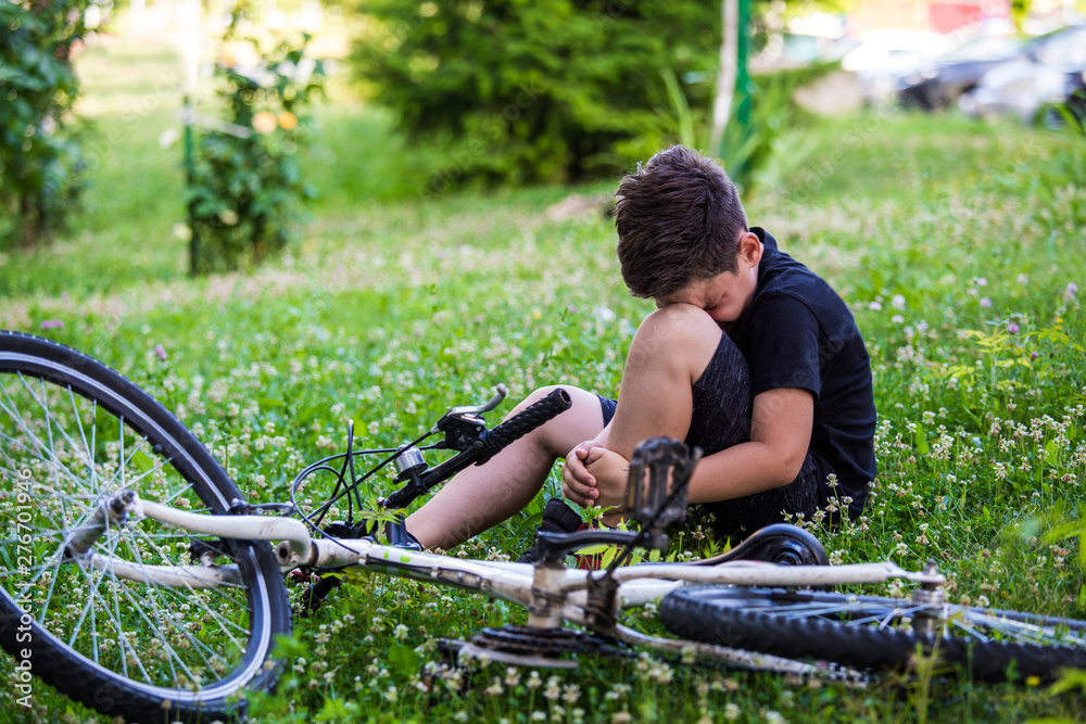 Boy in the street ground with a knee injury screaming after falling off ...
