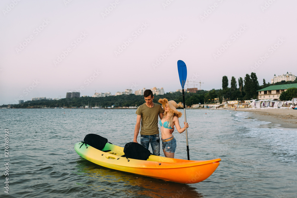 the ocean shore, a loving couple are knee-deep in water, a kayak floats ...