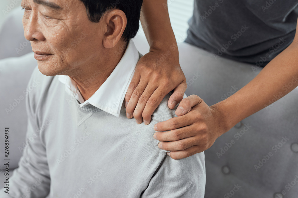 Asian old man shoulder pain, sitting on sofa , son massaging father ...