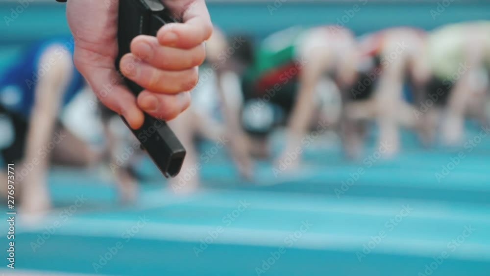Referee's hand with starting pistol on blurred background of athletes ...