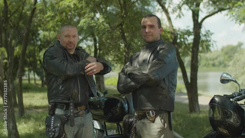 Serious brutal male bikers in leather jackets with arms crossed posing ...