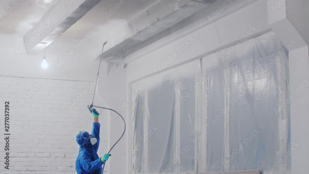 Worker painting the ceiling by airless spray gun with white color ...