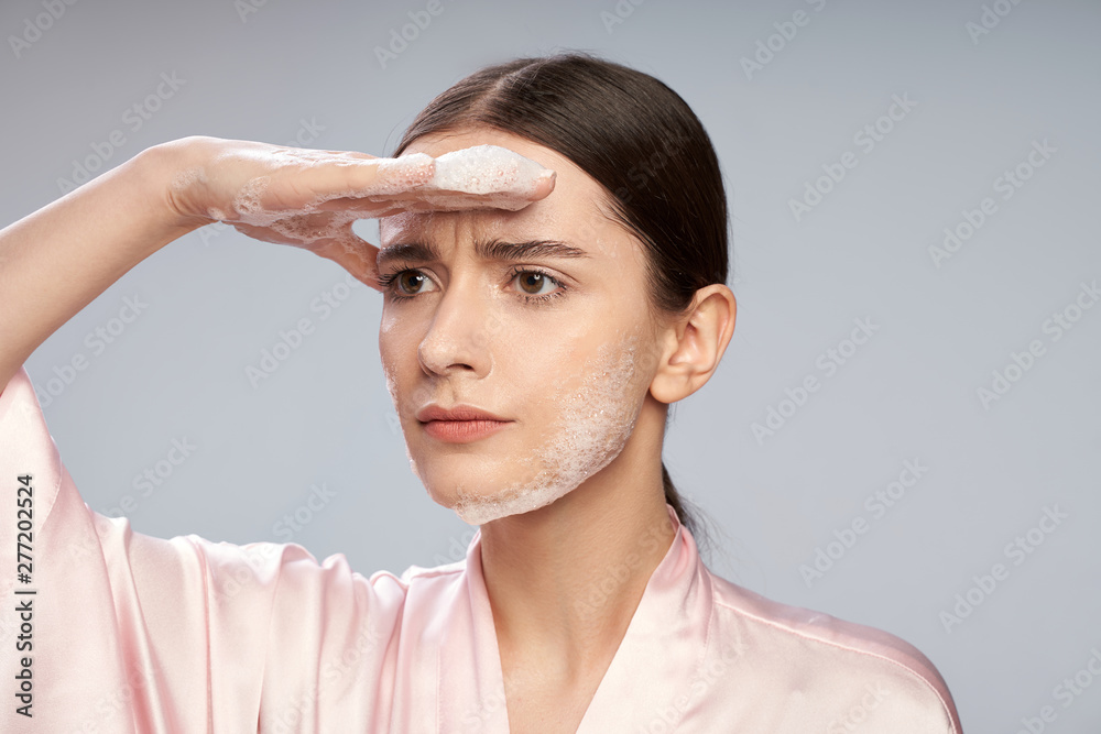 Beautiful girl with purifying foam on face keeping hand on forehead ...