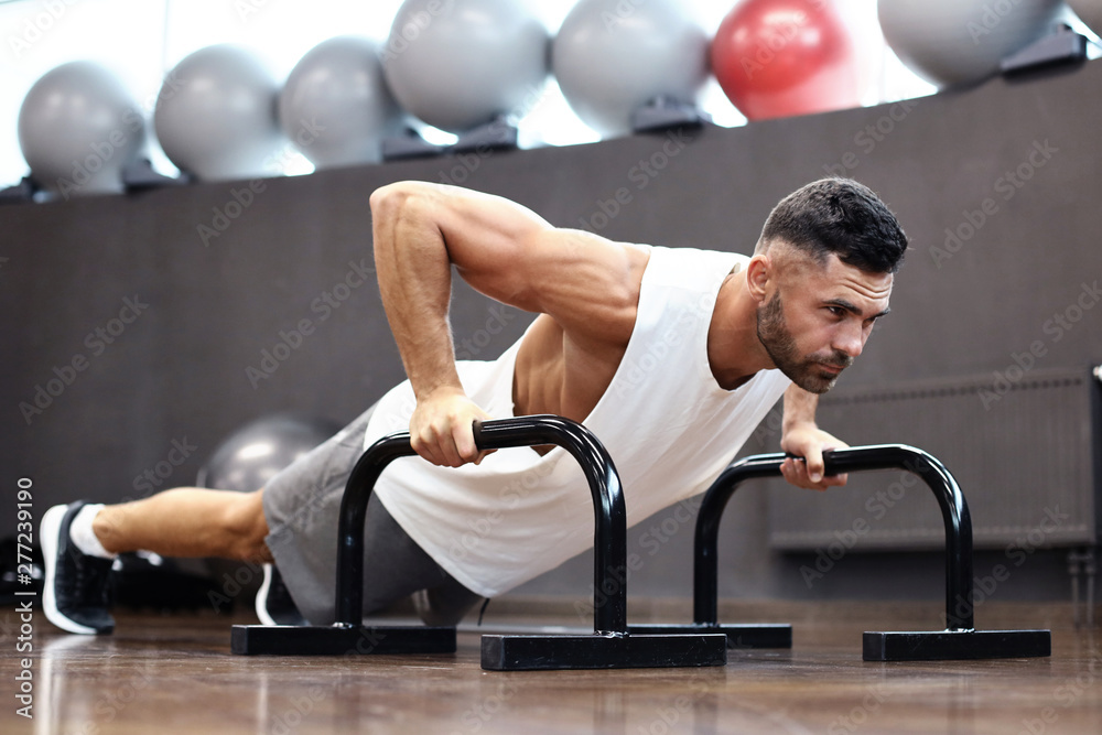 Fit and muscular man doing horizontal push-ups with bars in gym. Stock ...