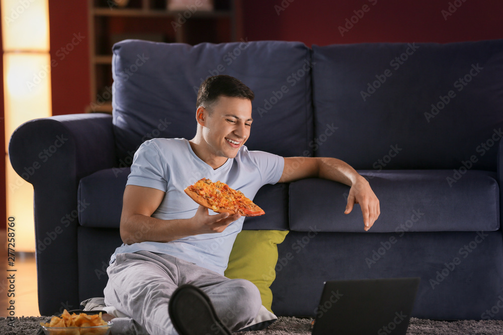 Handsome young man eating unhealthy food while watching movie at night ...