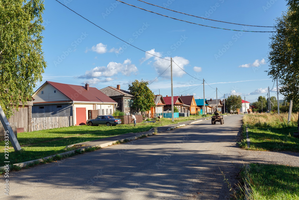Russian village in summer. View of the village road with traditional wooden houses along the ...