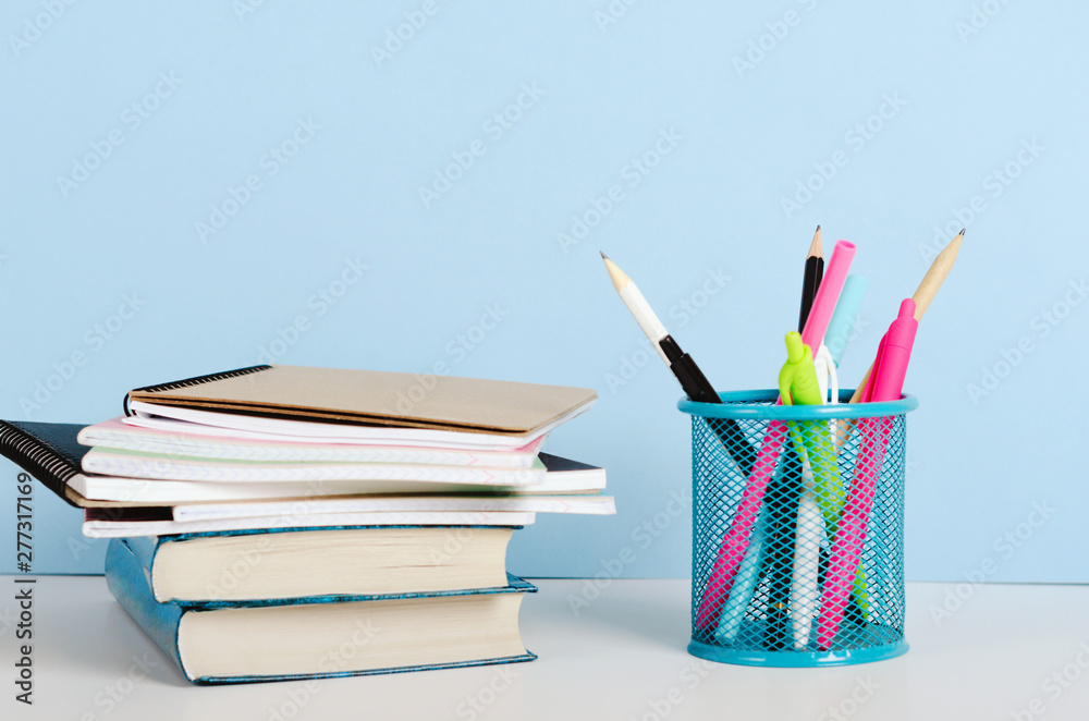 Multi-colored pencils, pens in a stand and books with notebooks on a ...