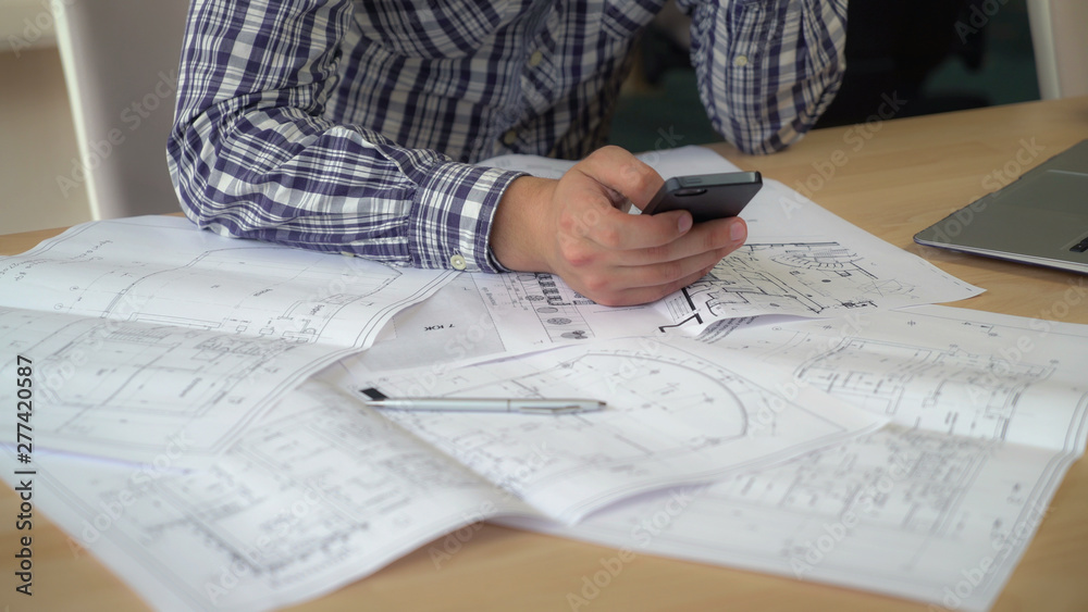 Designer using mobile phone works with plan building. take photo of ...