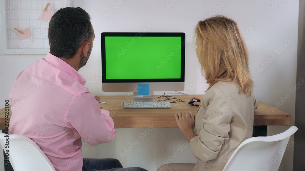 Business people sitting at the desk in front of computer with green ...