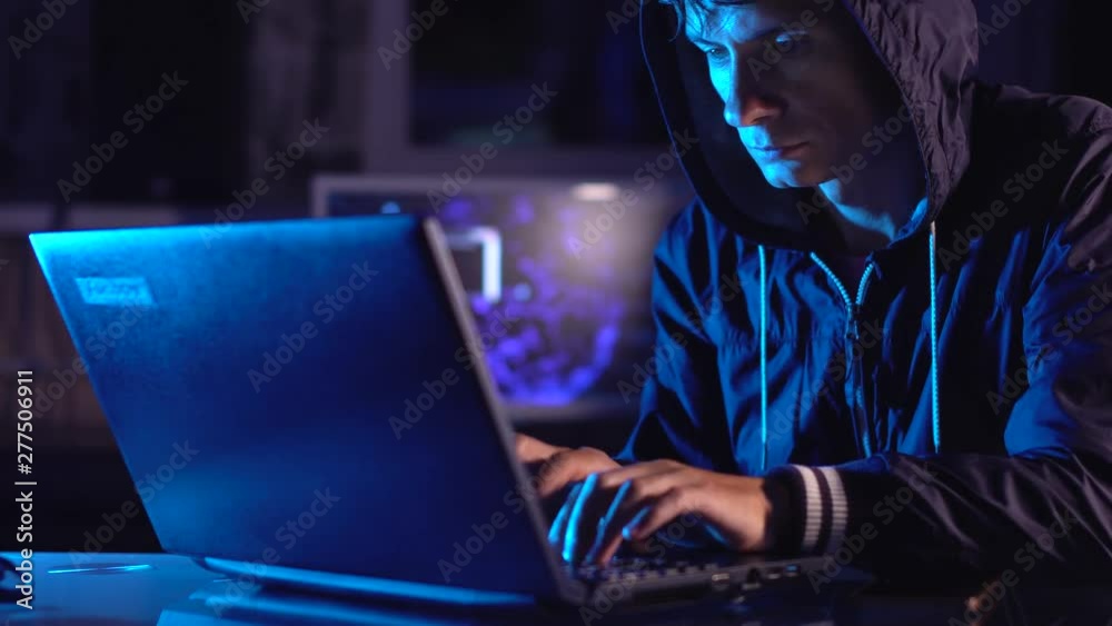 Hacker typing program code while committing a cybercrime hacking a system firewall in the dark ...
