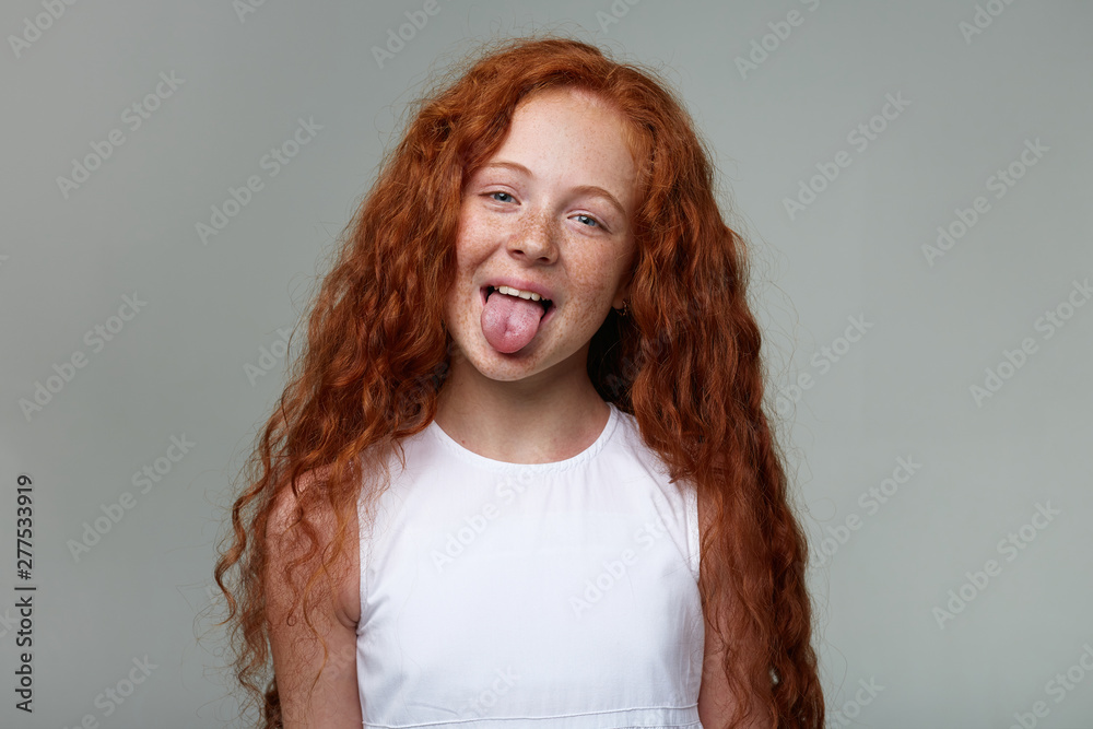 Photo of funny little girl with ginger hair and freckles, shows tongue ...