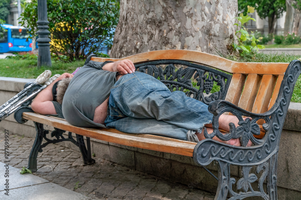 homeless man with a big belly sleeping on a wooden bench on a sunny day ...