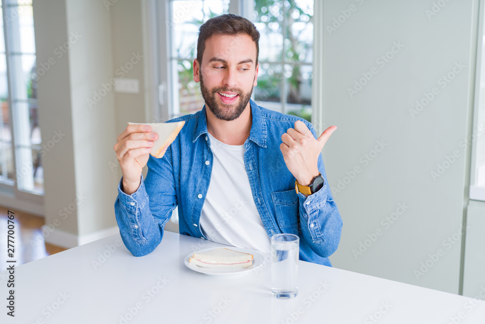 Handsome man eating healthy sandwich pointing and showing with thumb up ...