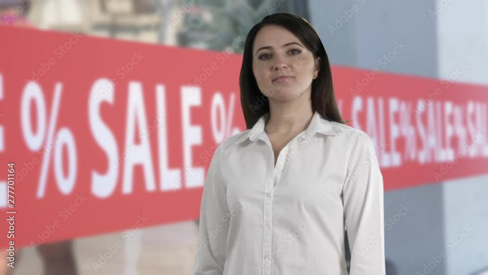 Confident woman standing against shop window display with text Sale on ...