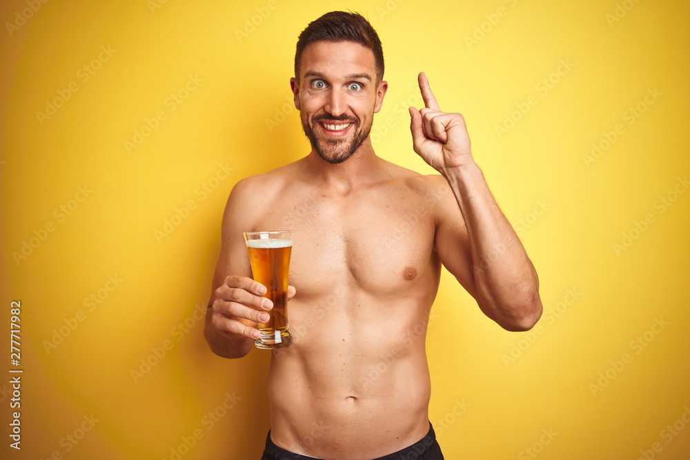 Young handsome shirtless man drinking a pint of beer over isolated ...