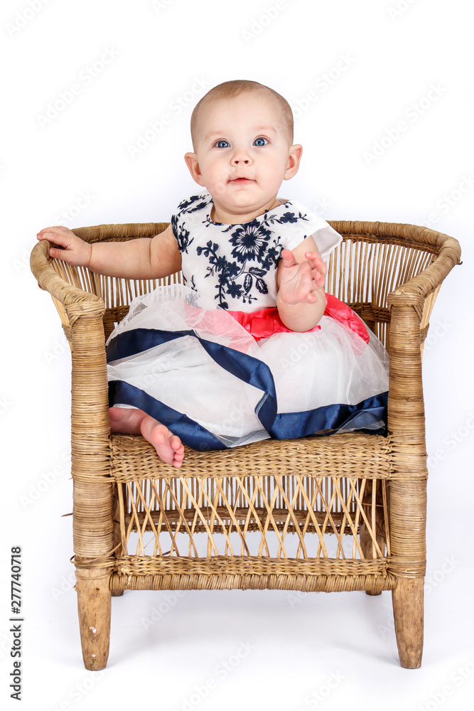 Little girl/baby sitting on a small wicker/rattan/cane chair in studio ...