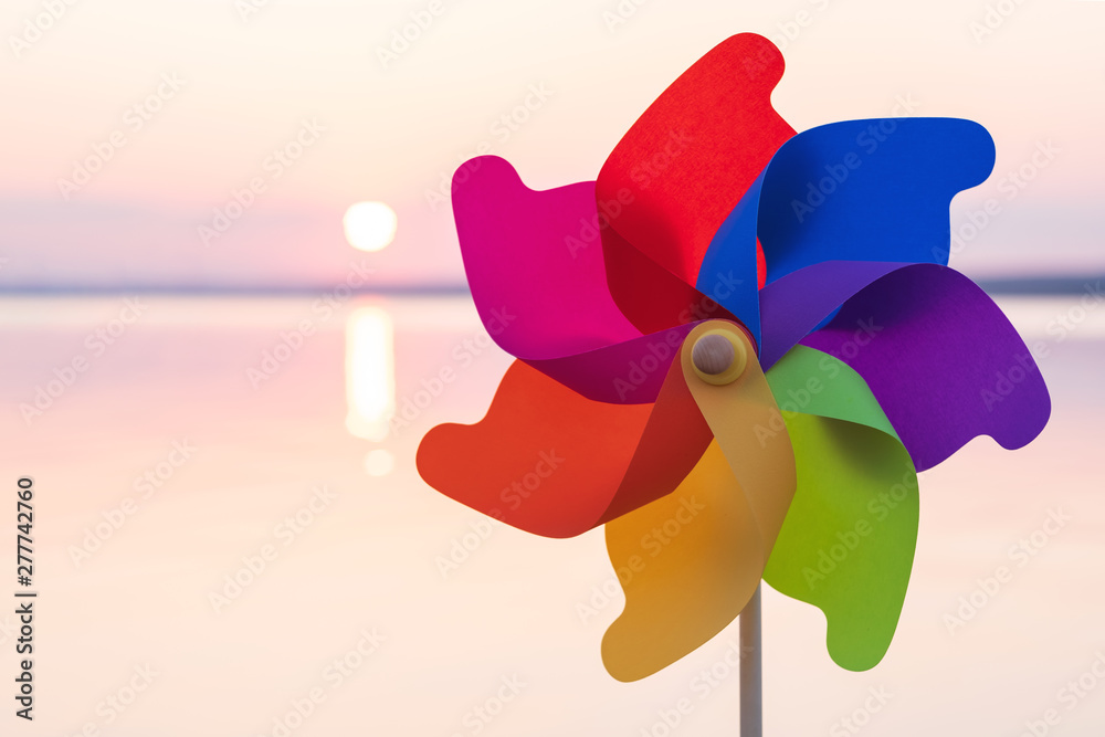 A round colored plastic pinwheel with a blowing wind stands on the sand ...