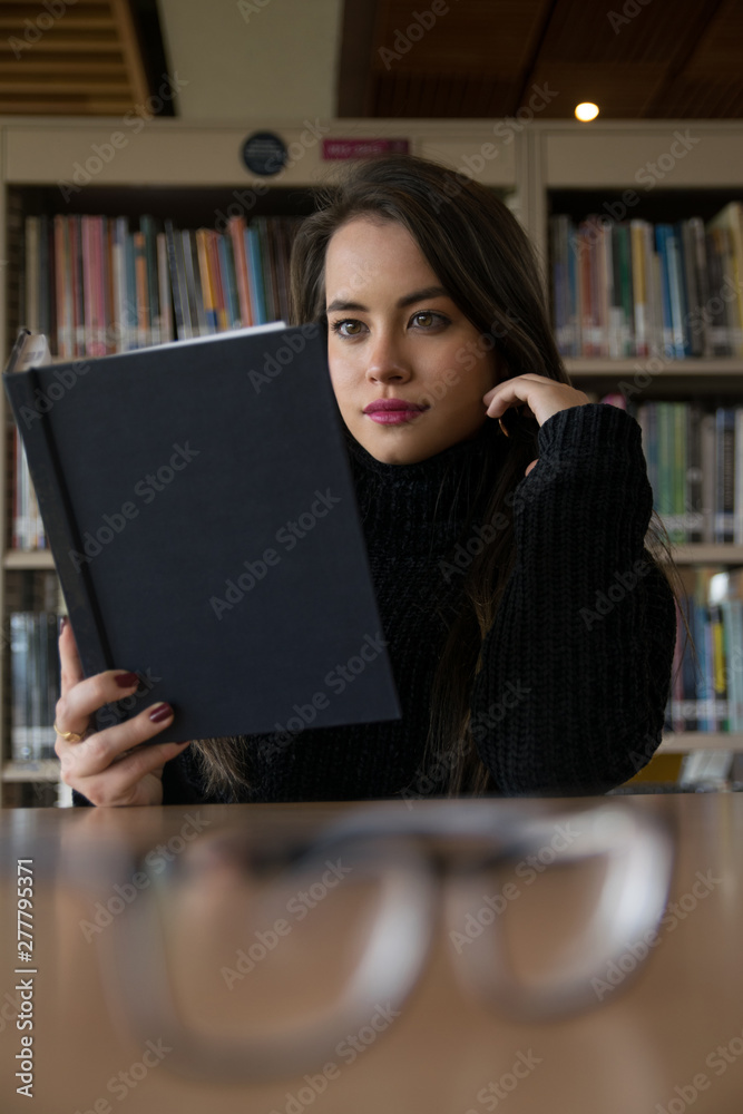 Pretty woman sitting along bookshelves and holding open book Stock ...