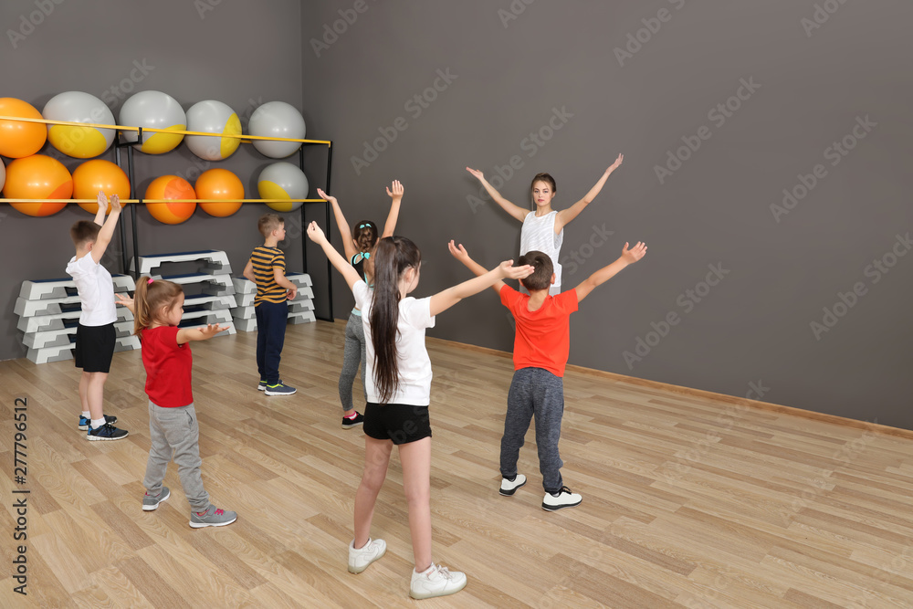 Cute little children and trainer doing physical exercise in school gym ...