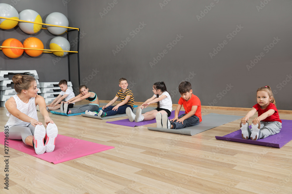Cute little children and trainer doing physical exercise in school gym ...