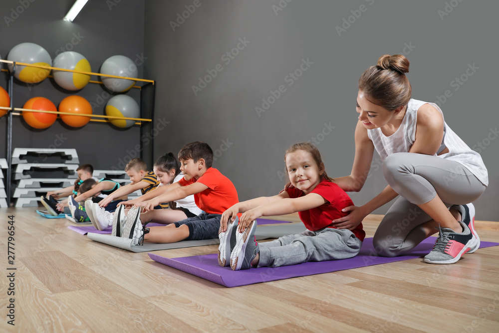 Trainer helping children to do physical exercise in school gym. Healthy ...