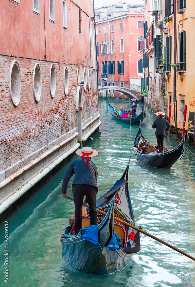 Venetian gondolier punting gondola through green canal waters of Venice ...