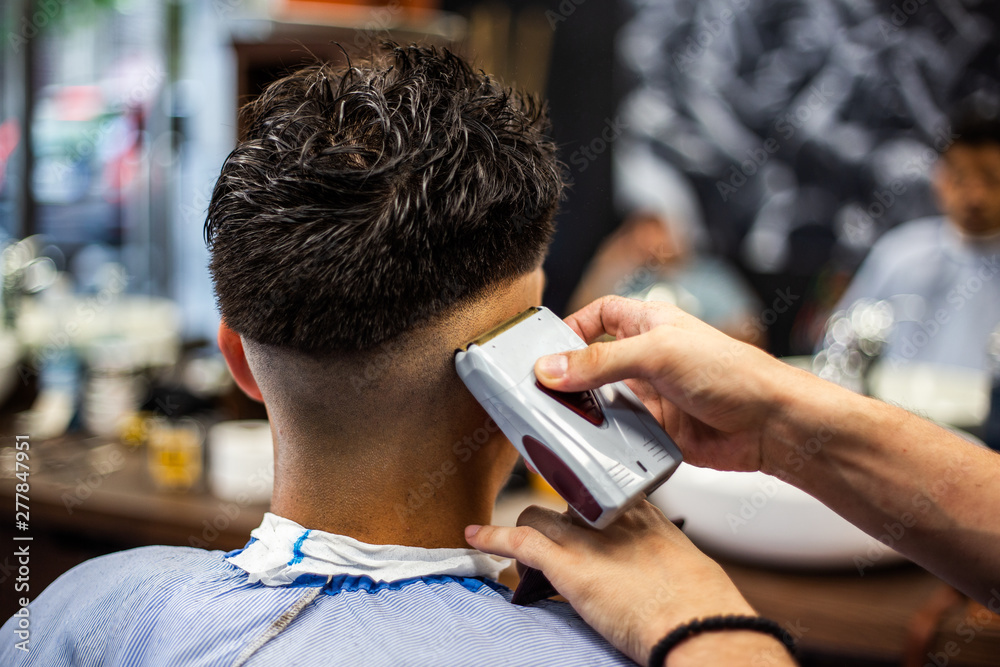 Rear view of young man getting a modern haircut. Man being trimmed with ...