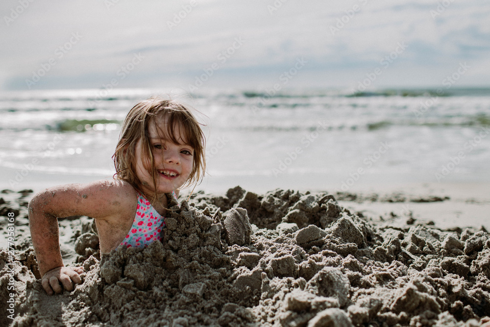 young girl buried in the sand smiling at the beach Stock Photo | Adobe ...