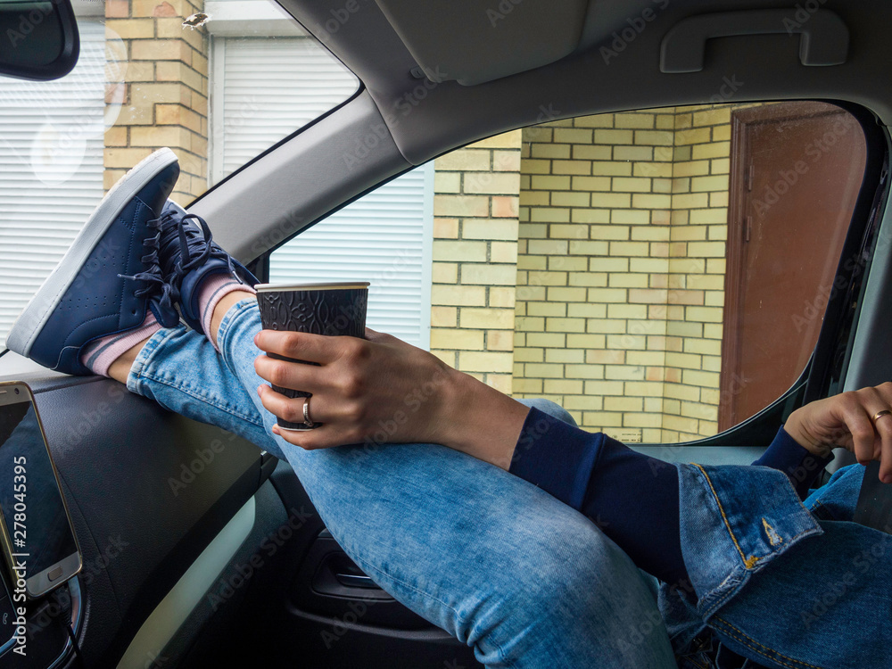 Young drinking coffee take away with feet in boots on car dashboard ...