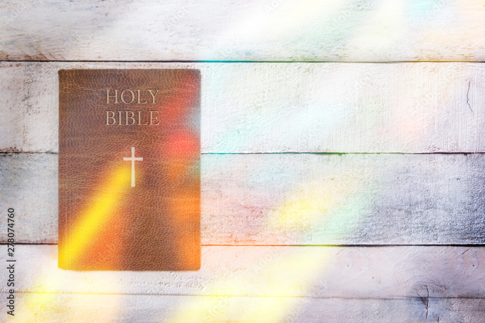 Holy Bible with some stained glass reflection on a wooden table. Top ...
