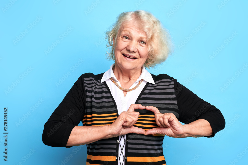 Beautiful old woman making heart gesture isolated over blue background ...