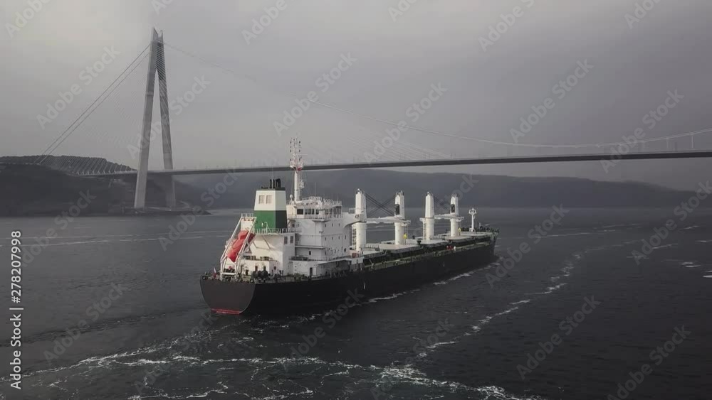 A bulk carrier ship with deck cranes, sails into the strait. Cargo ship ...