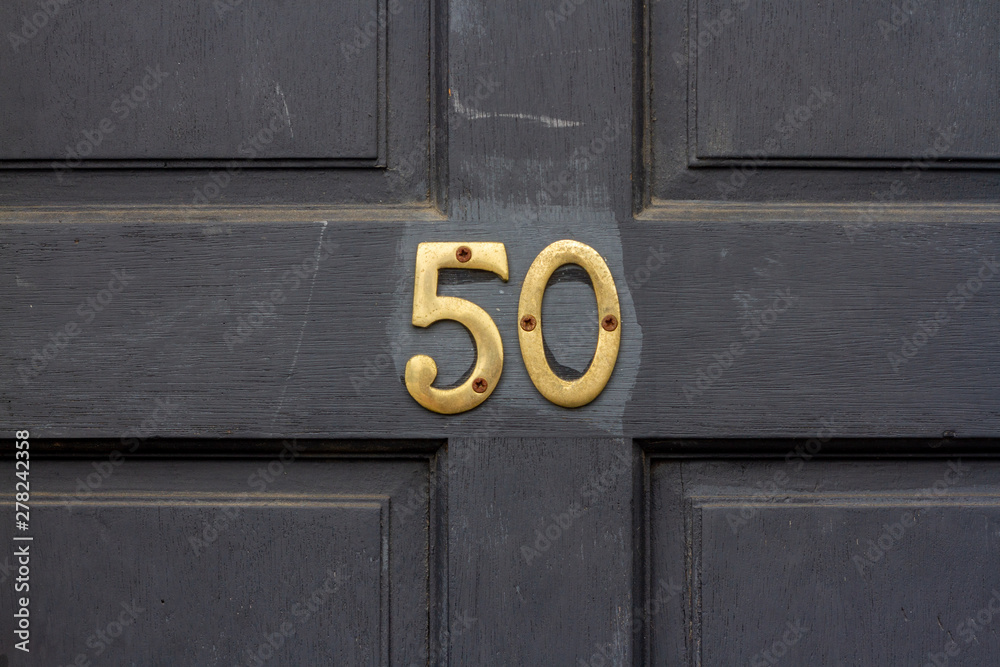 HOuse number 50 with the fifty in bronze on an old black wooden front ...