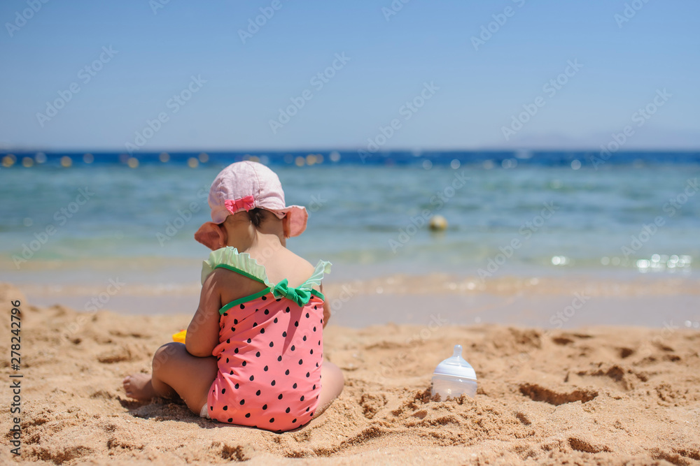 back view photo of a little girl in swimsuit and pink hat sitting on ...