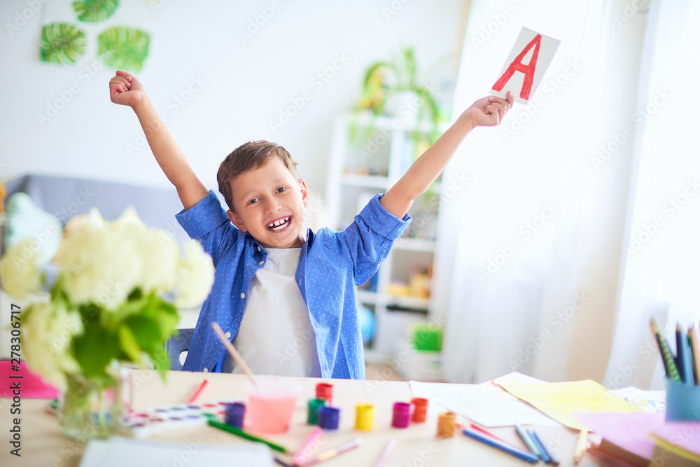 happy child at the table with school supplies smiles funny and learns ...