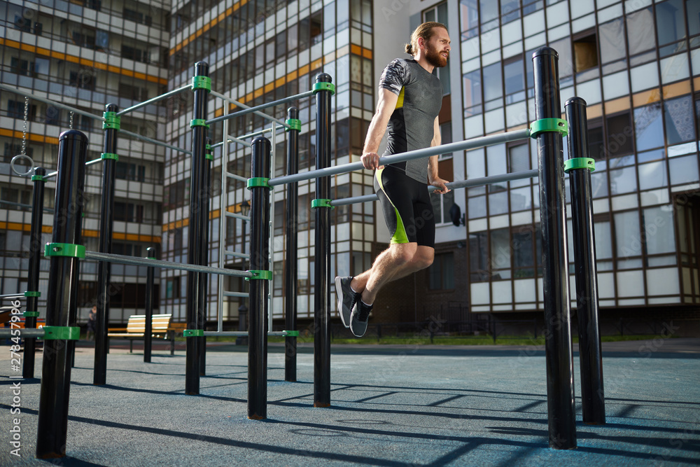 Tireless muscular athlete with red beard hanging on parallel bars while ...