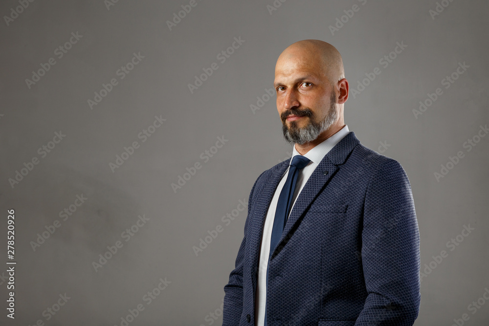 Cute young bald bearded businessman in a classic suit on a gray ...